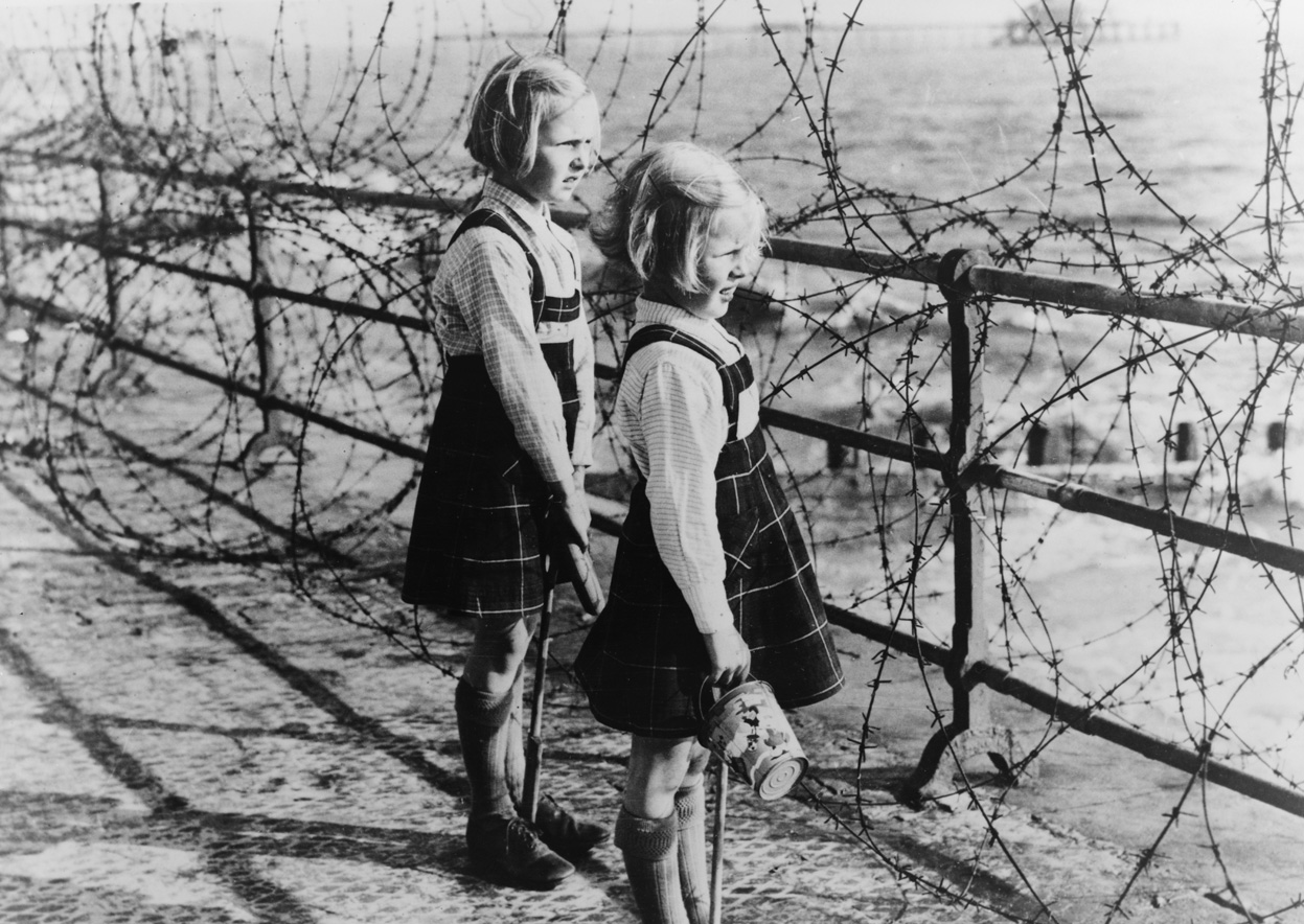 Asisbiz Battle Of Britain Twogirlslookouttowardthebeachthroughanewlyconstructedbarbed